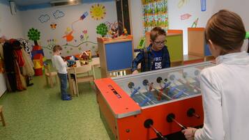 Uma sala de jogos infantil com mesa de pebolim, brinquedos e decorações educativas nas paredes.
