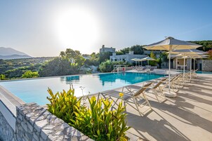 Uma piscina com espreguiçadeiras e guarda-sóis, rodeada por paredes de pedra e vegetação.