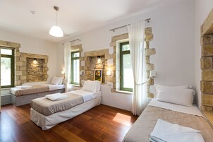Quarto com três camas, paredes de pedra, piso de madeira e janelas amplas com cortinas.