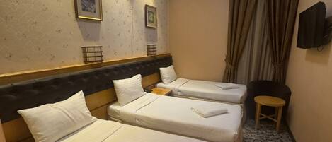 Quarto de hotel com duas camas, uma mesa pequena, televisão e um carpete estampado.
