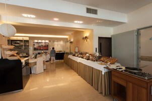 Buffet montado com diversas opções de comida, alguém servindo e uma área de cozinha com fogão.