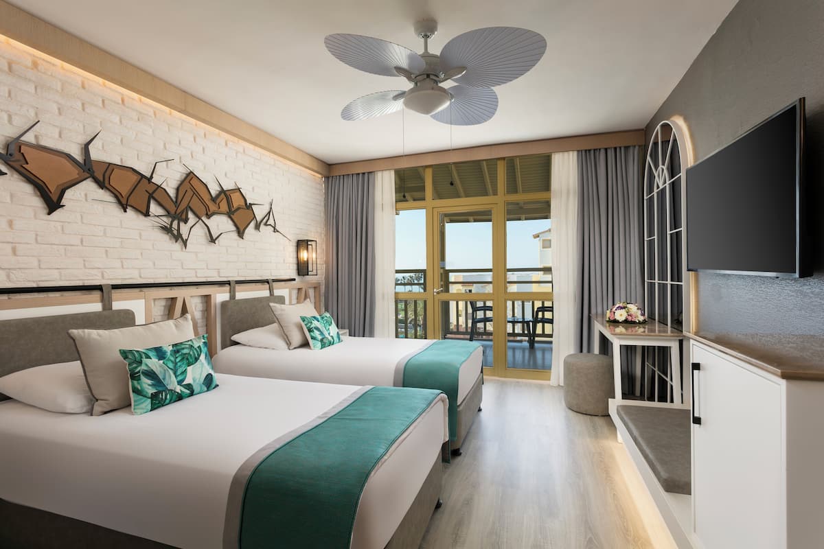 Quarto de hotel com duas camas, um ventilador de teto, televisão e varanda com vista.