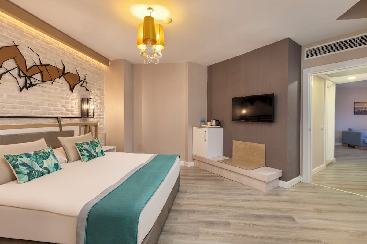 Quarto de hotel moderno com uma cama grande, televisão de tela plana, um detalhe decorativo na parede e um pequeno espaço para sentar.