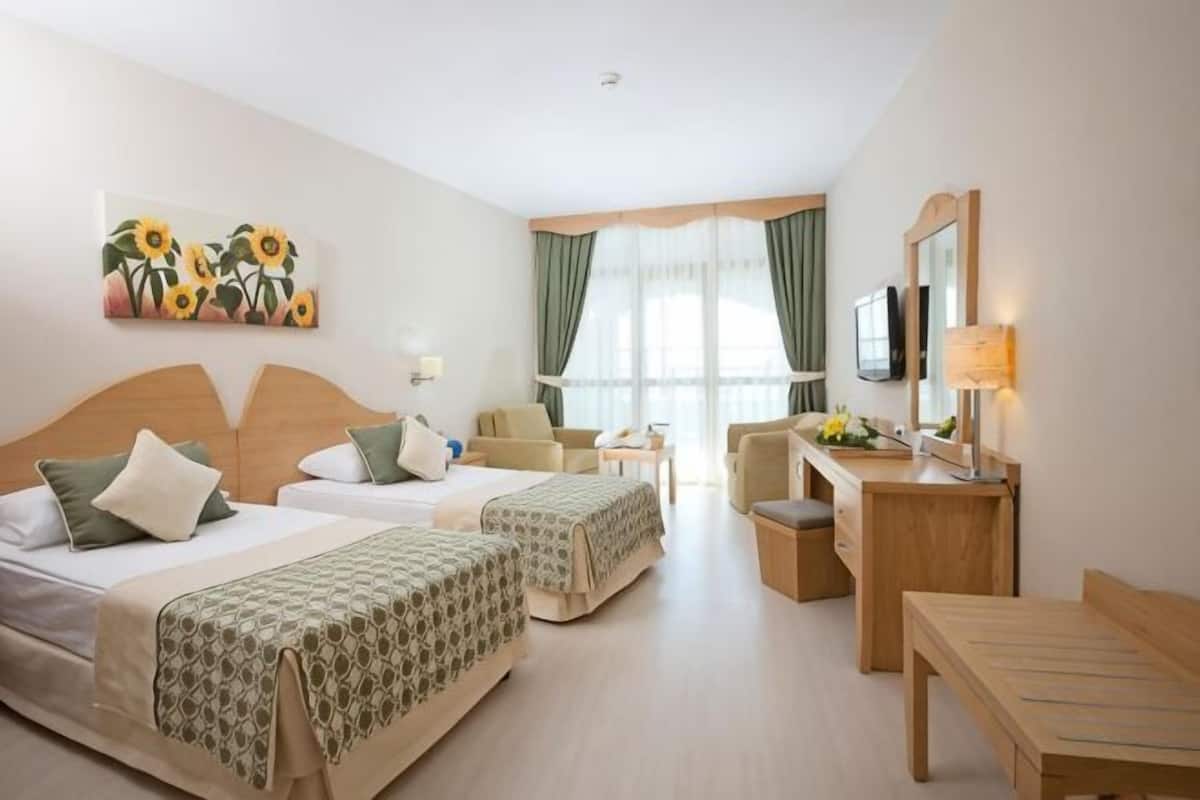 Quarto de hotel com duas camas, uma escrivaninha, uma cadeira, uma televisão e uma janela com cortinas.