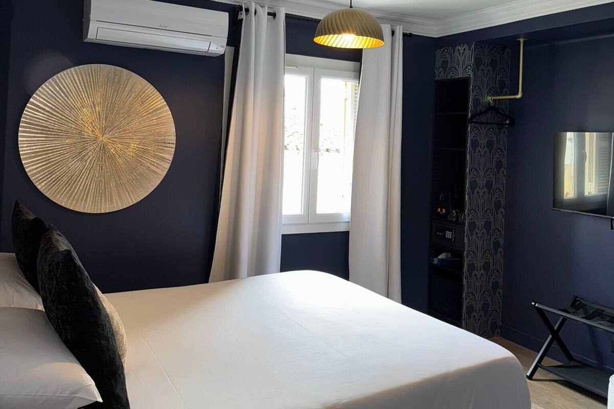 Quarto com cama, ar condicionado, luminária pendente e televisão na parede.