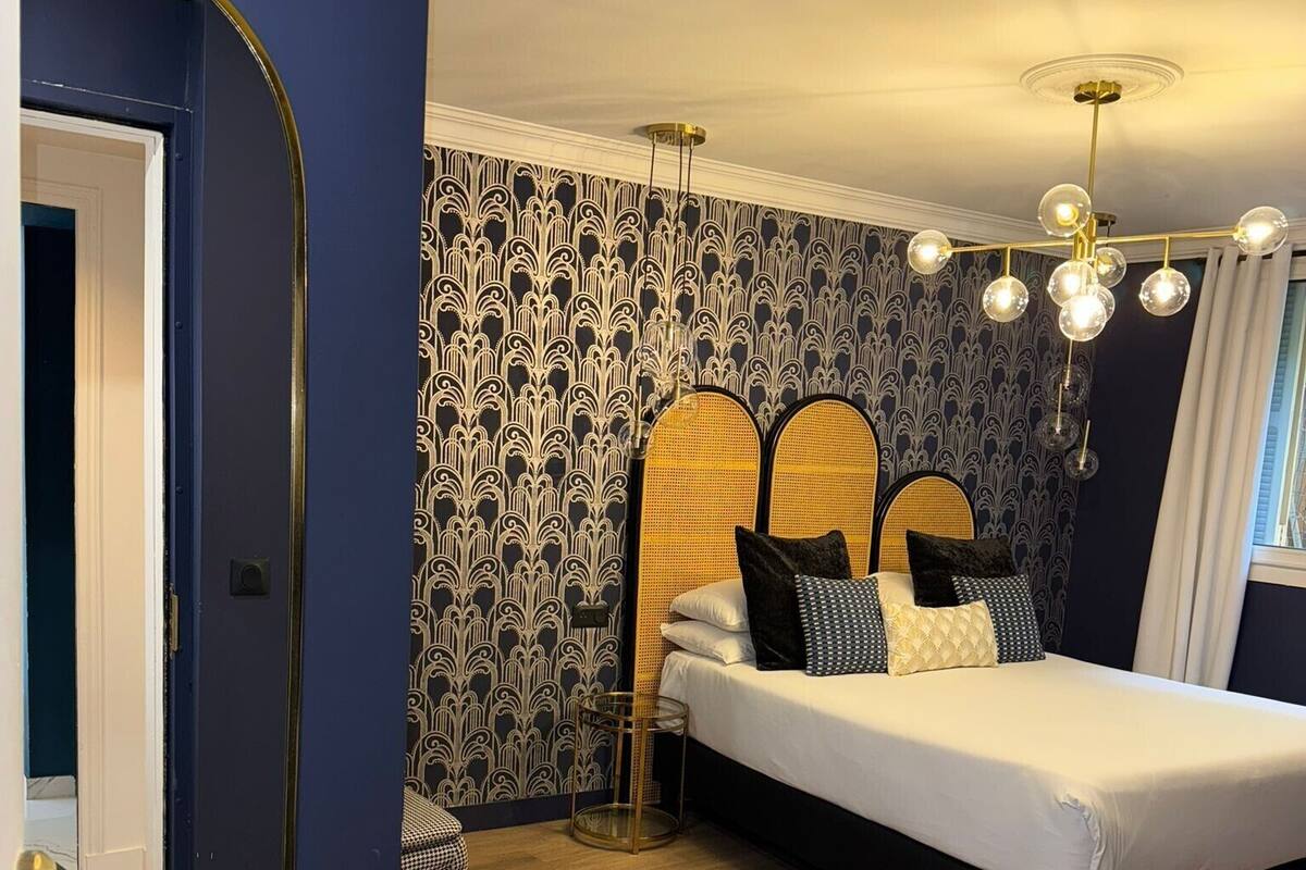 Um quarto com uma cama grande, um espelho, uma parede com papel de parede estampado e uma luminária no teto.