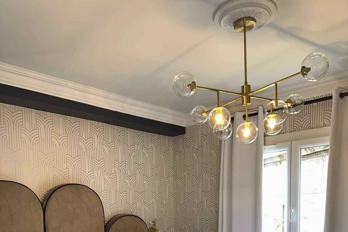 Quarto com uma cama grande, um candelabro moderno e papel de parede estampado.
