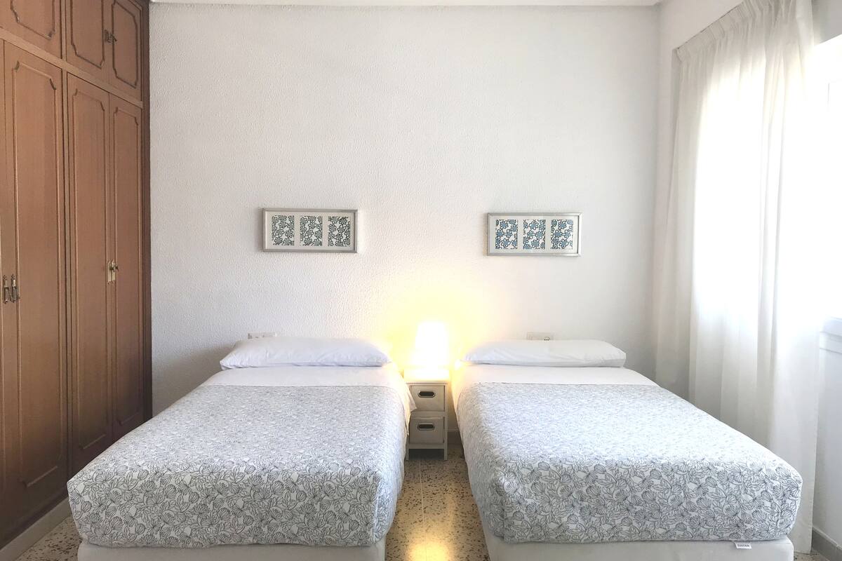 Quarto com duas camas de solteiro, um guarda-roupa de madeira e dois quadros na parede.