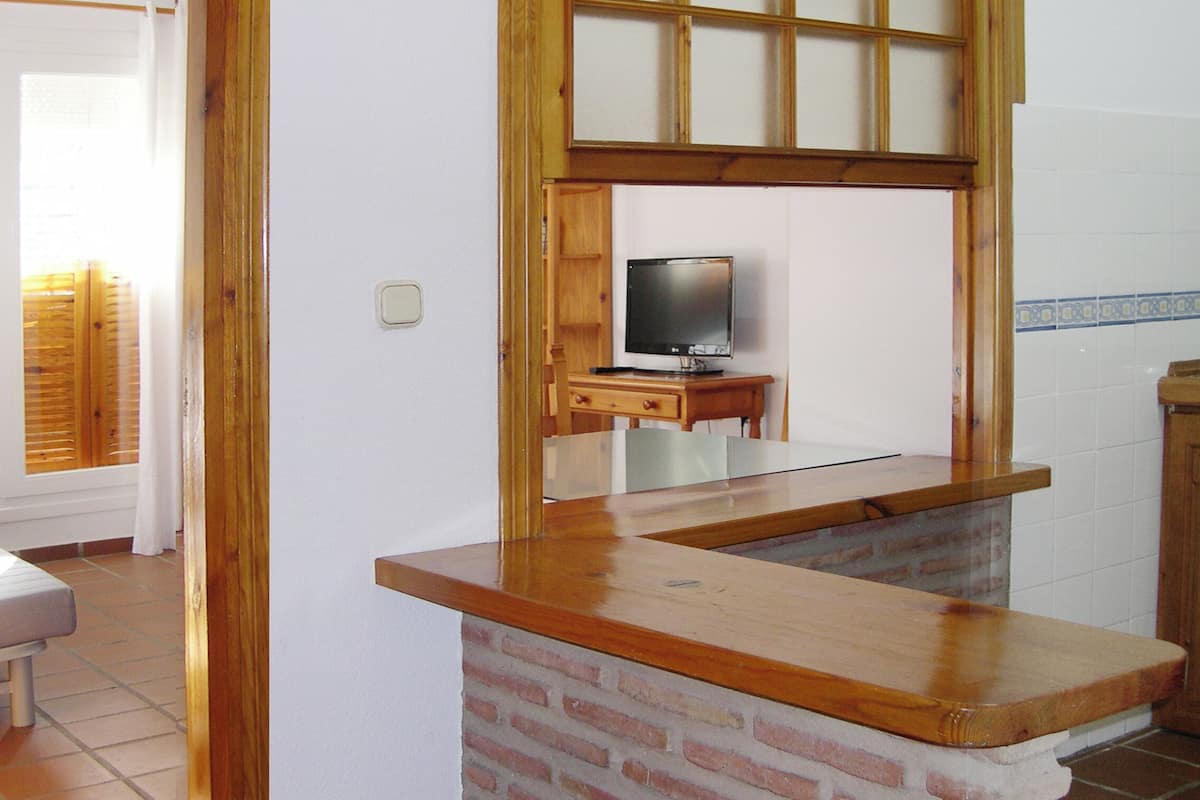 Uma cozinha com bancada de madeira, parede de tijolos, televisão sobre suporte de madeira e janela com persianas.