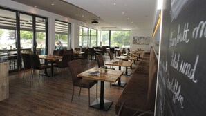 Restaurante moderno com mesas e cadeiras de madeira, janelas amplas e um cardápio em lousa.
