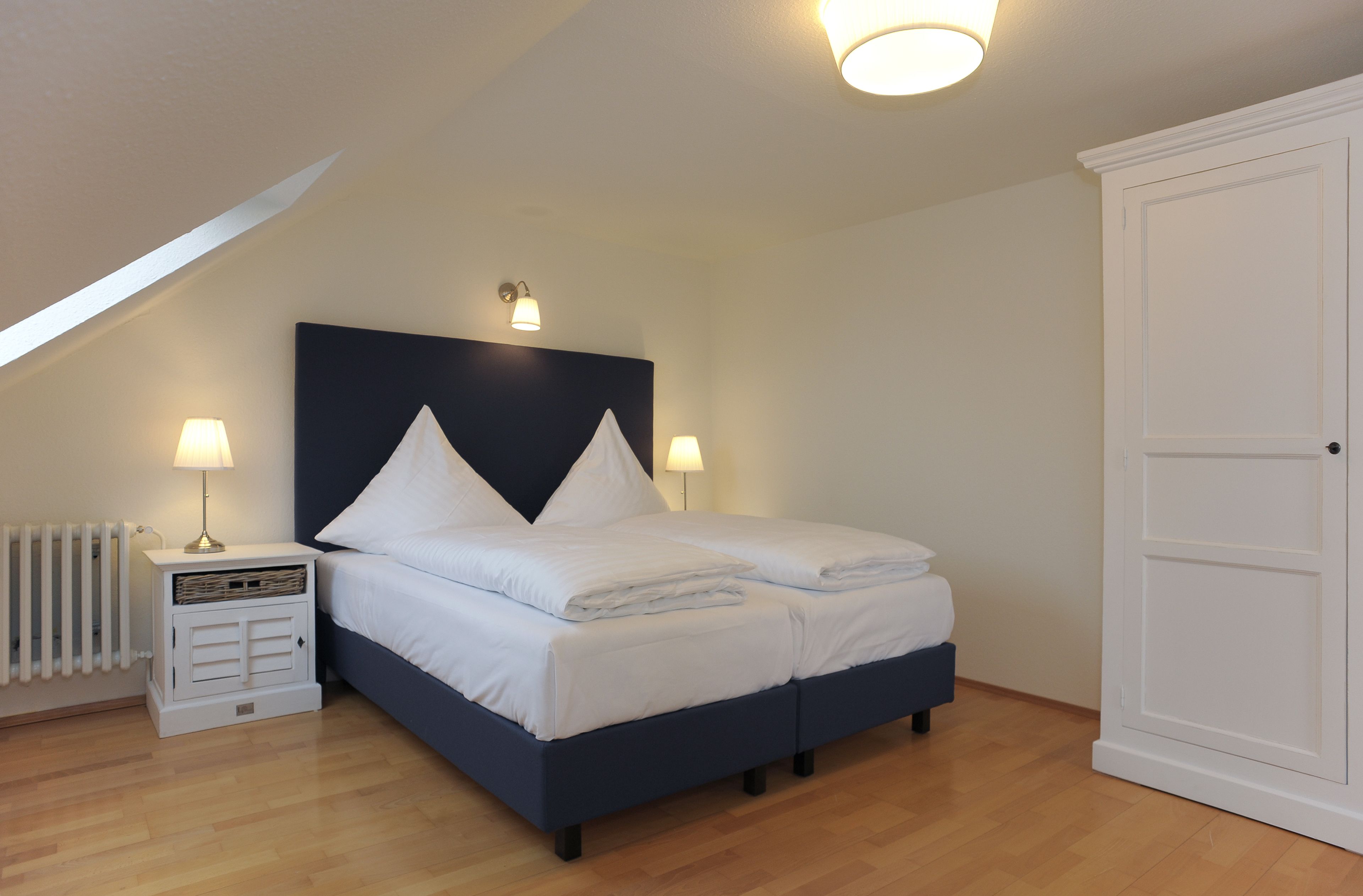 Um quarto com cama, luminárias de cabeceira, um radiador e um guarda-roupa.