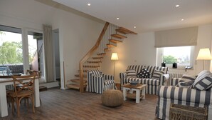 Uma sala de estar ampla com escada de madeira, sofás listrados e uma área de jantar com cadeiras de madeira.