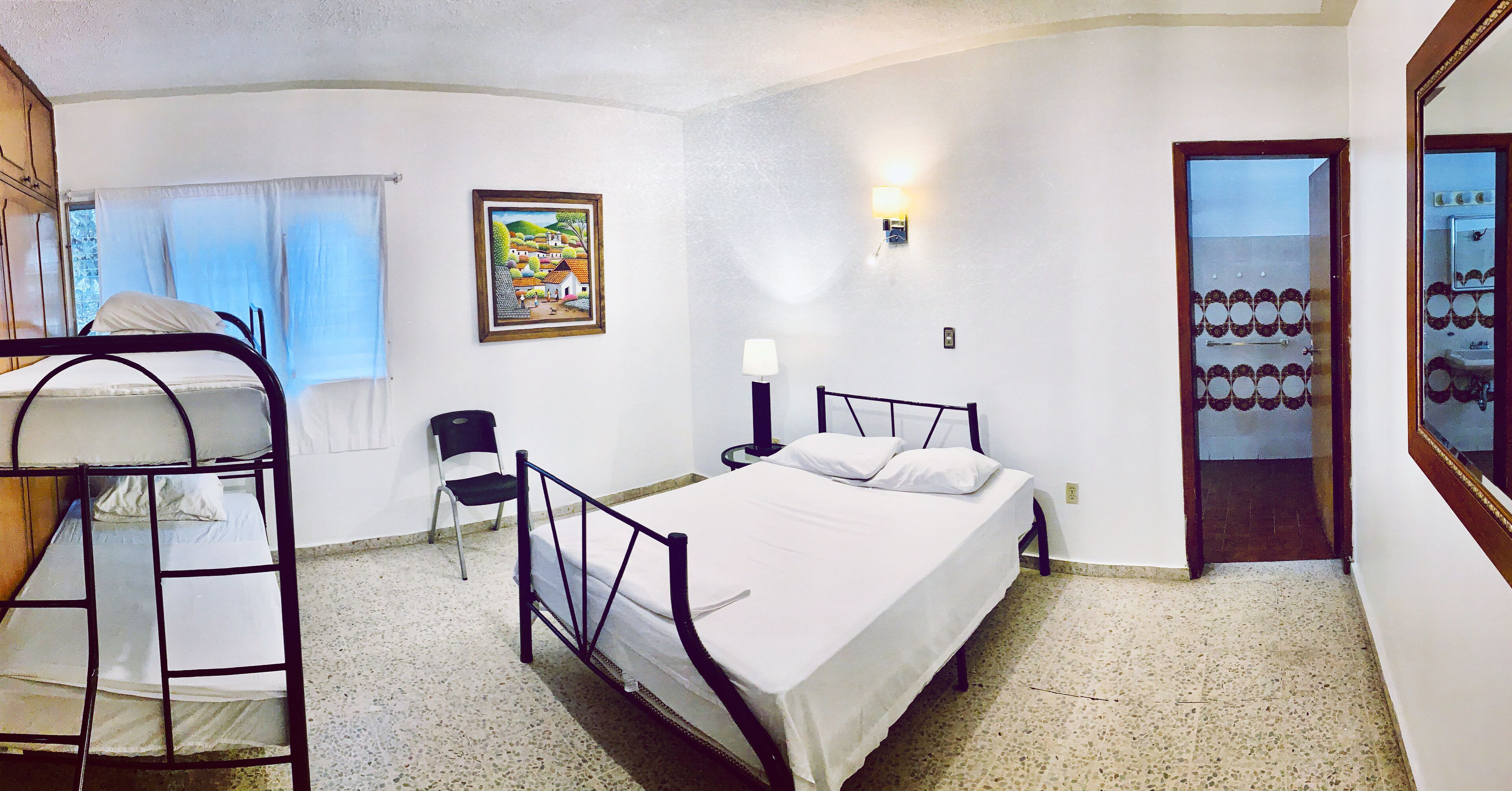 Um quarto com cama, uma cadeira, uma escrivaninha, um abajur e um quadro na parede.