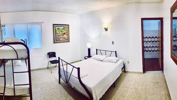 Um quarto com cama, uma cadeira, uma escrivaninha, um abajur e um quadro na parede.