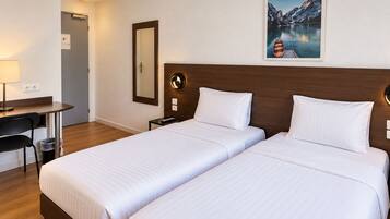 Quarto de hotel com duas camas, uma escrivaninha, uma cadeira, um cesto de lixo, uma mesa de cabeceira e um espelho fixado na parede.