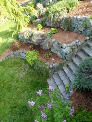 Um jardim ajardinado com degraus de pedra, diversos arbustos e flores de lilás.