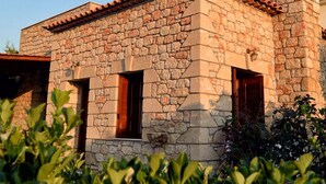 Um edifício de pedra com telhado em telhas e duas janelas com persianas.