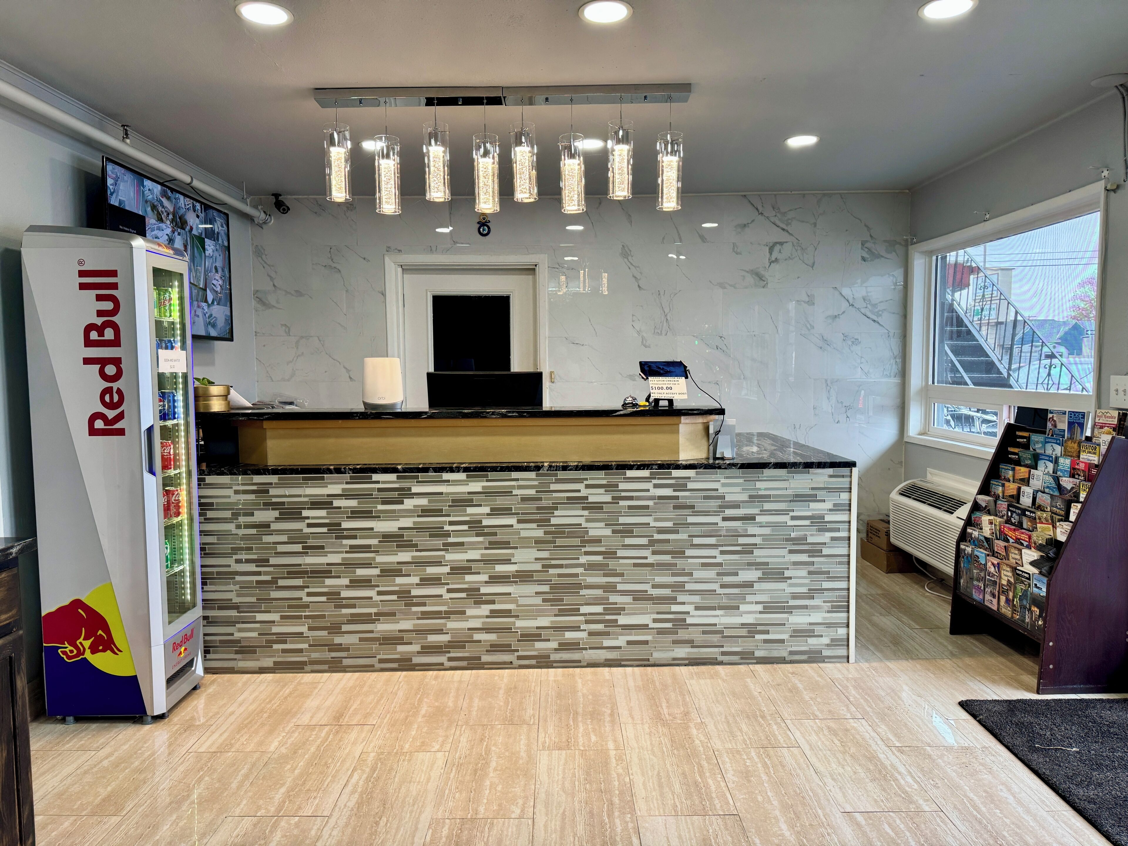 Uma área de recepção com parede de mármore, máquina de venda automática da Red Bull, balcão revestido em azulejos e janela com vista.
