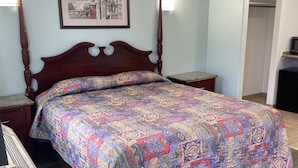 Um quarto com uma cama de dossel de madeira, um edredom colorido, duas mesas de cabeceira, um quadro na parede e uma porta que dá para outro cômodo.