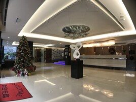 Um saguão de hotel moderno com uma árvore de Natal, um balcão de recepção e uma grande escultura abstrata.
