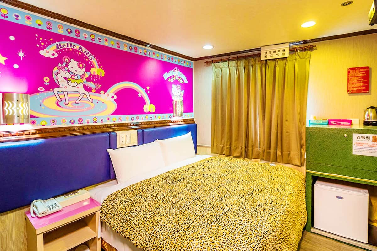 Quarto de hotel com uma cama, uma escrivaninha, um telefone, um armário verde e uma cortina.