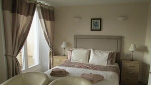 Quarto de hotel com cama, duas mesas de cabeceira, duas luminárias, uma cadeira e uma janela com cortinas.