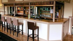 Uma área de bar com balcão extenso, vários bancos e uma variedade de garrafas e copos.