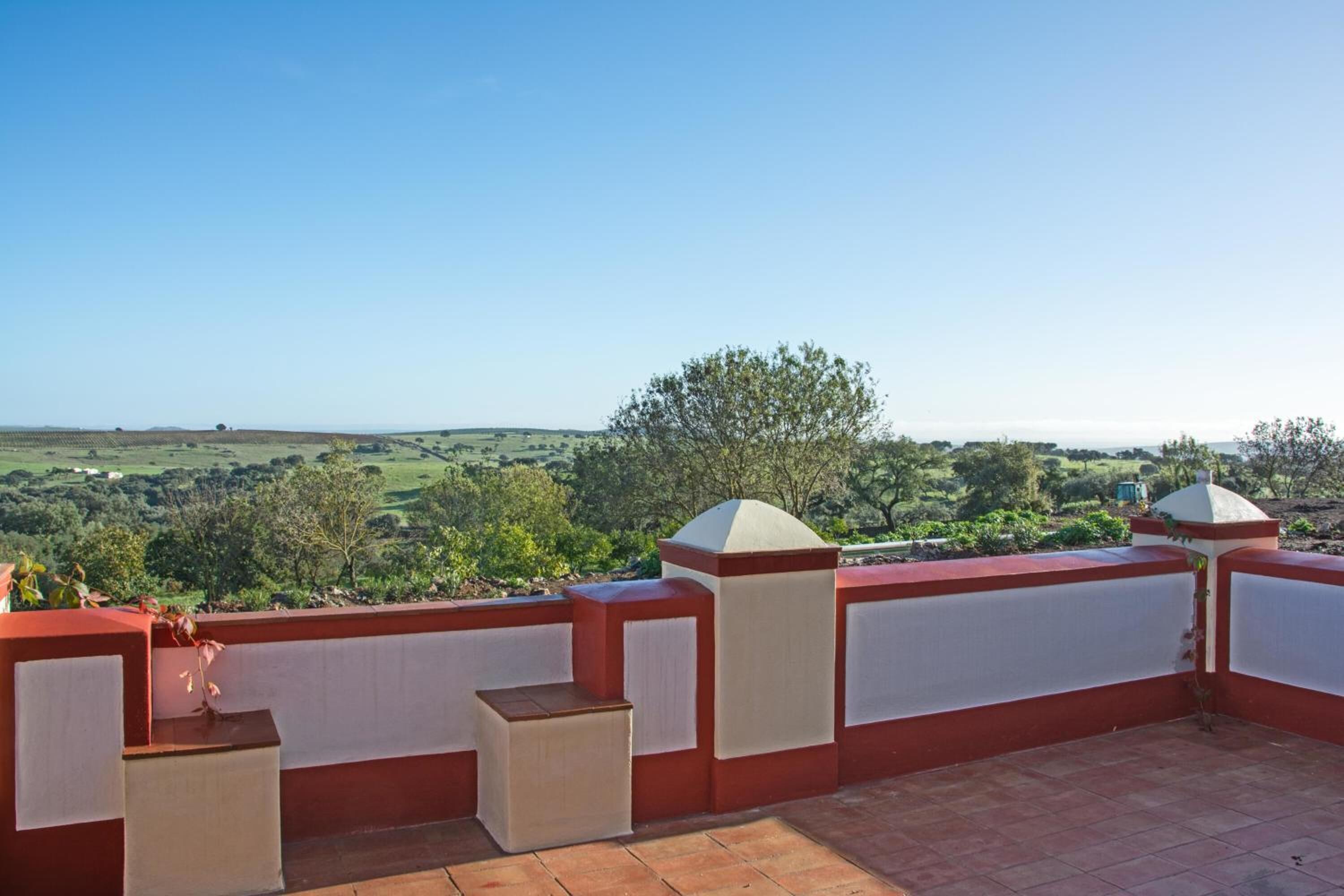 Terraço com parede vermelha e branca, uma mesa pequena e um banco.