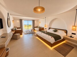 Quarto de hotel moderno com cama grande, área de estar com vista e mesa de jantar.