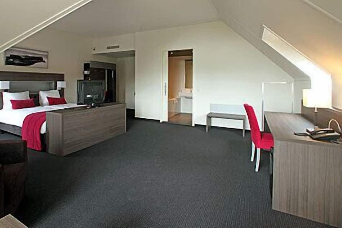 Quarto de hotel moderno com cama, escrivaninha, cadeira e televisão.