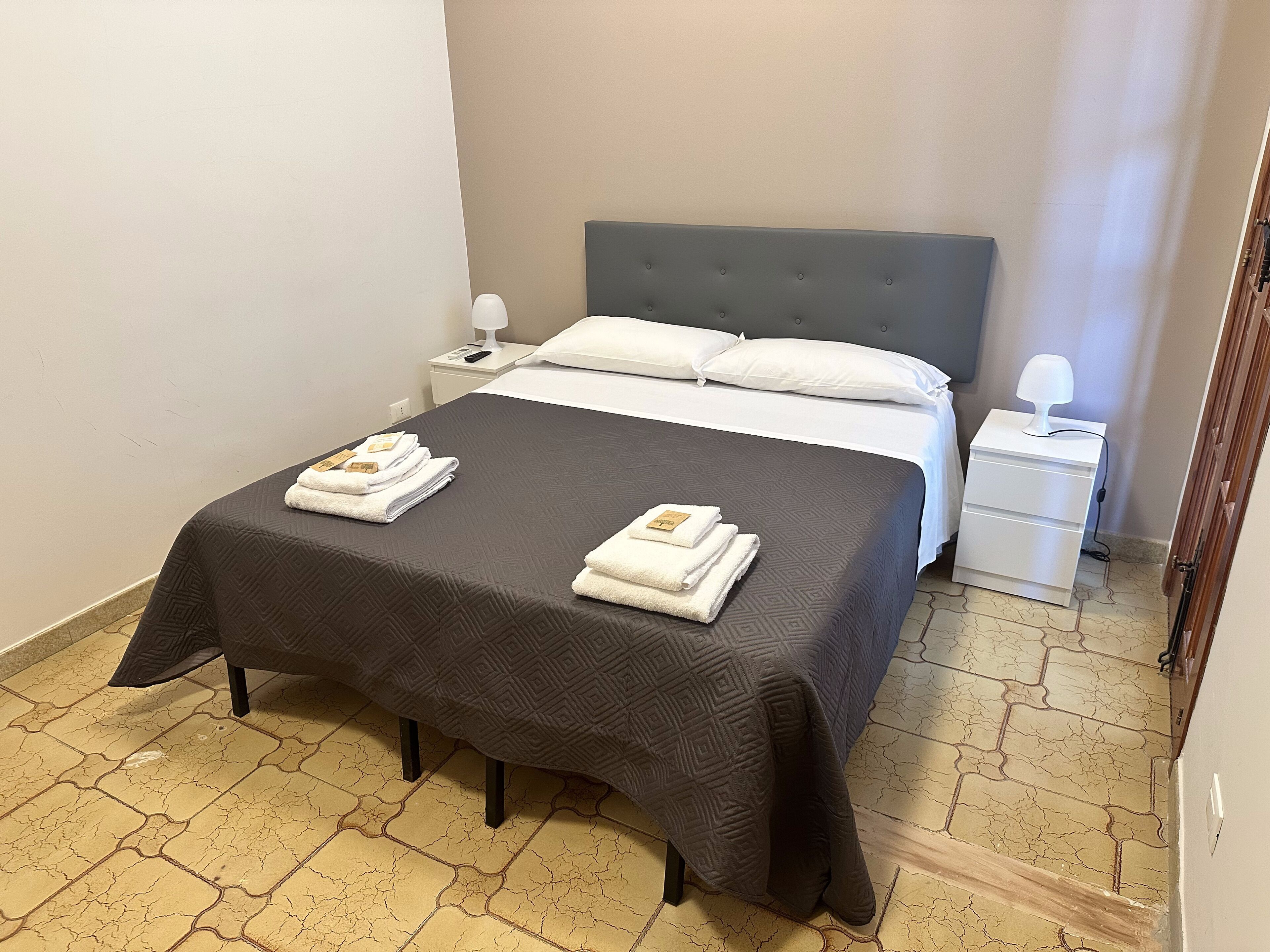 Quarto de hotel com uma cama, duas mesas de cabeceira e uma luminária.