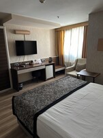 Quarto de hotel com uma cama grande, uma escrivaninha com televisão de tela plana, um sofá e uma mesinha.