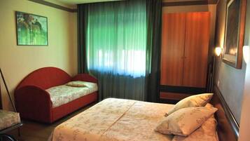 Quarto de hotel com cama, sofá vermelho, quadro na parede e janela com cortinas.