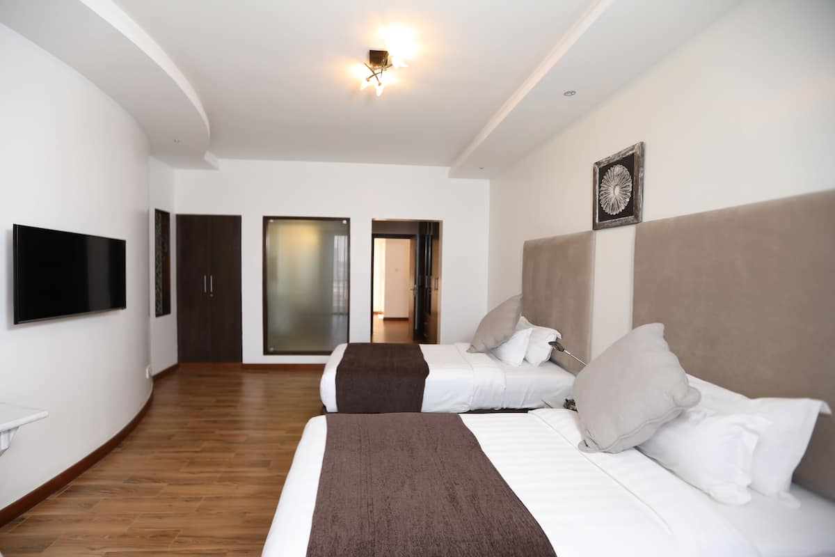 Quarto de hotel com duas camas, televisão de tela plana, um espelho grande e uma porta deslizante para um banheiro.