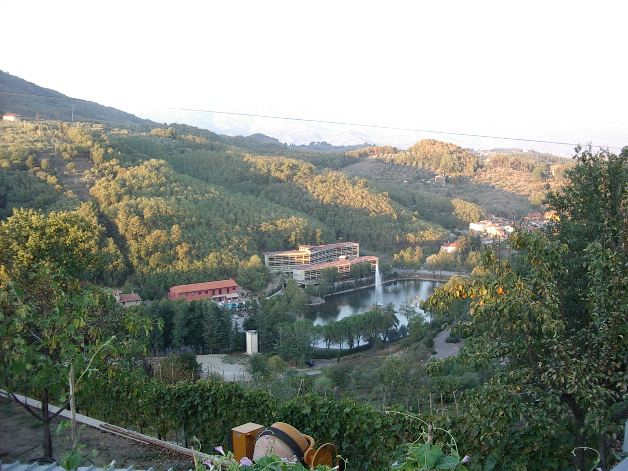 Vista de um vale com um edifício rodeado por vegetação exuberante e um lago.