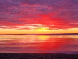 Pôr do sol sobre águas calmas, com horizonte nítido.