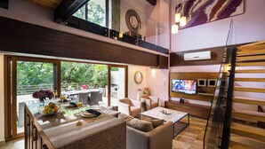 Uma sala de estar moderna com área de jantar de vidro, um sofá, uma mesa de centro e uma televisão.