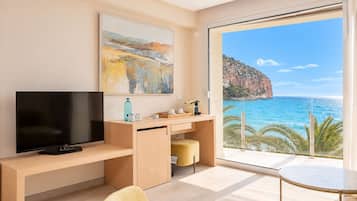 Quarto de hotel com televisão, escrivaninha, cadeira e uma grande janela com vista para o mar e falésias.