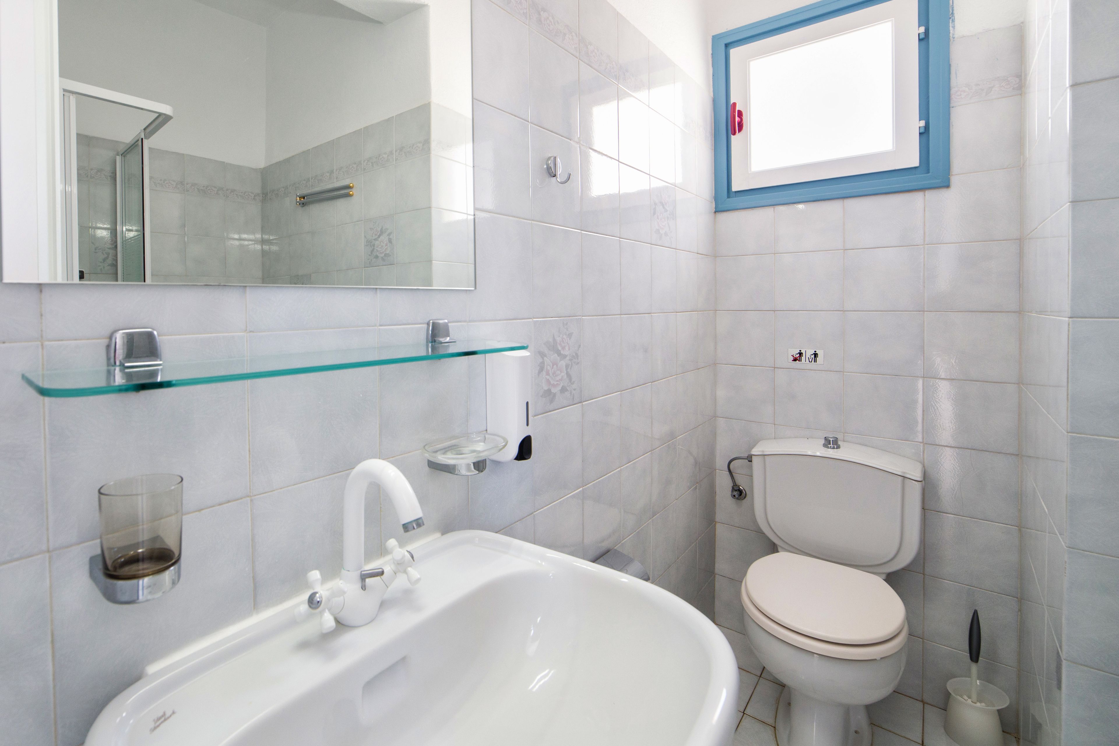 Casa de banho moderna com lavatório branco, prateleira de vidro e sanita.