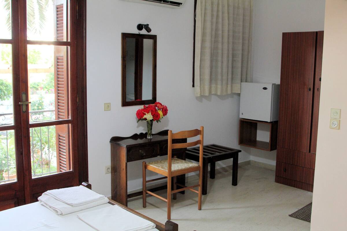 Quarto com cama, escrivaninha de madeira com cadeira, espelho, mesinha e guarda-roupa.