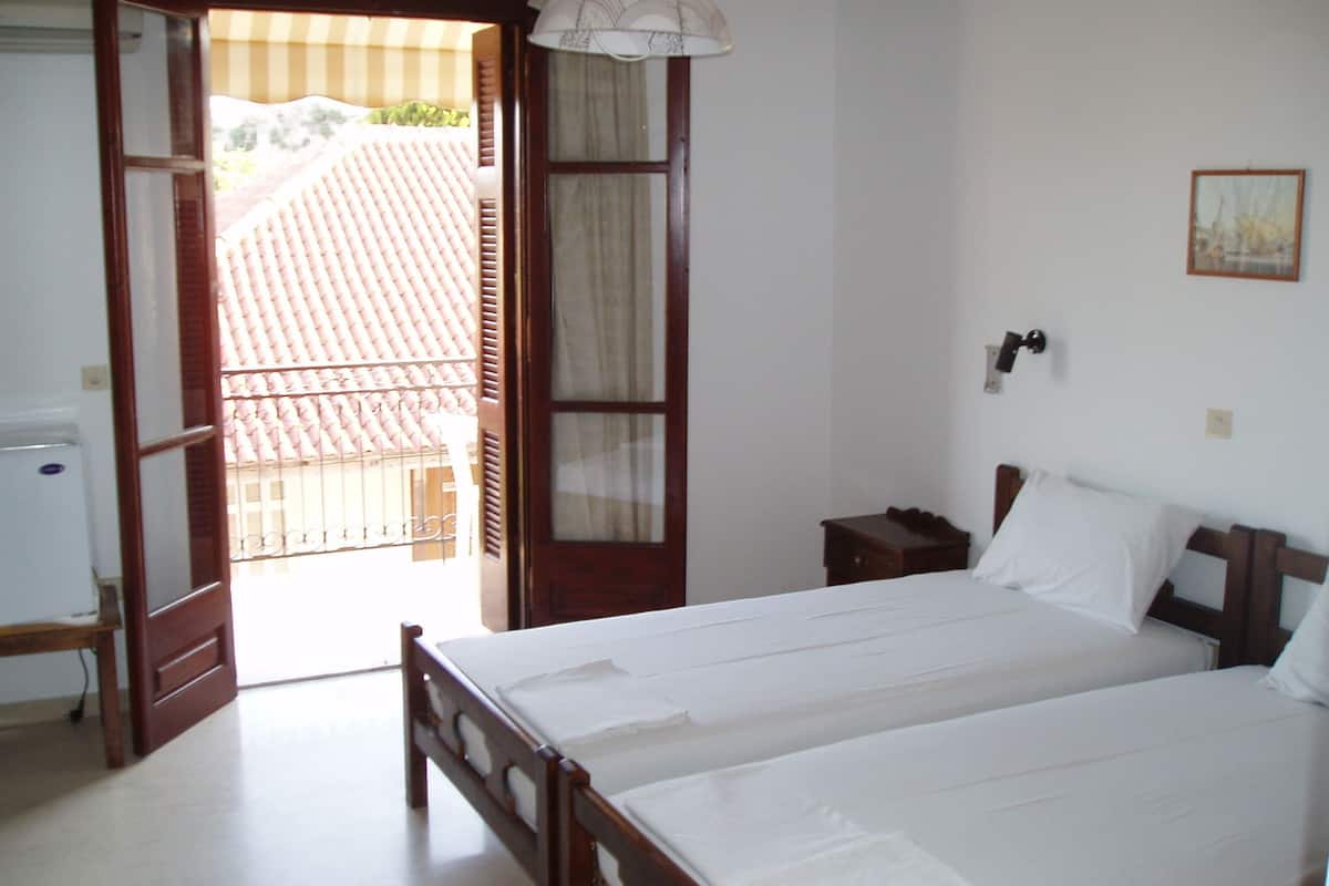 Quarto com uma cama de casal, mesa de cabeceira e porta que dá para uma varanda.