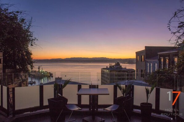 Terraço com mesa e cadeiras, com vista para a água ao pôr do sol.
