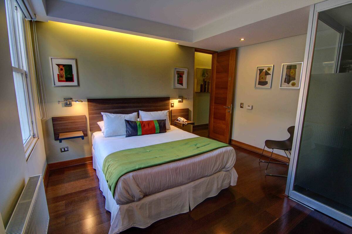 Quarto de hotel com uma cama grande, mesas de cabeceira, um espelho e uma porta de vidro deslizante.