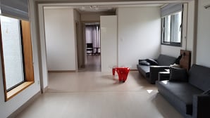 Uma sala de estar moderna com um sofá cinzento, uma mesa de centro vermelha e uma janela com persianas.