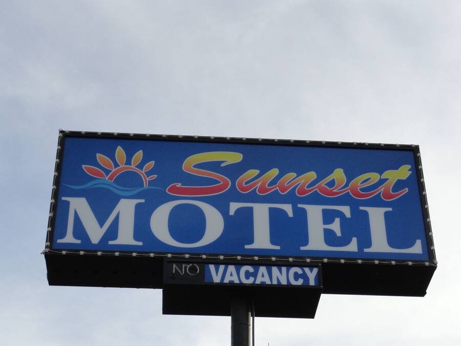 Placa de motel com o nome 'Sunset Motel' e um aviso de 'Sem Quartos Disponíveis' abaixo.