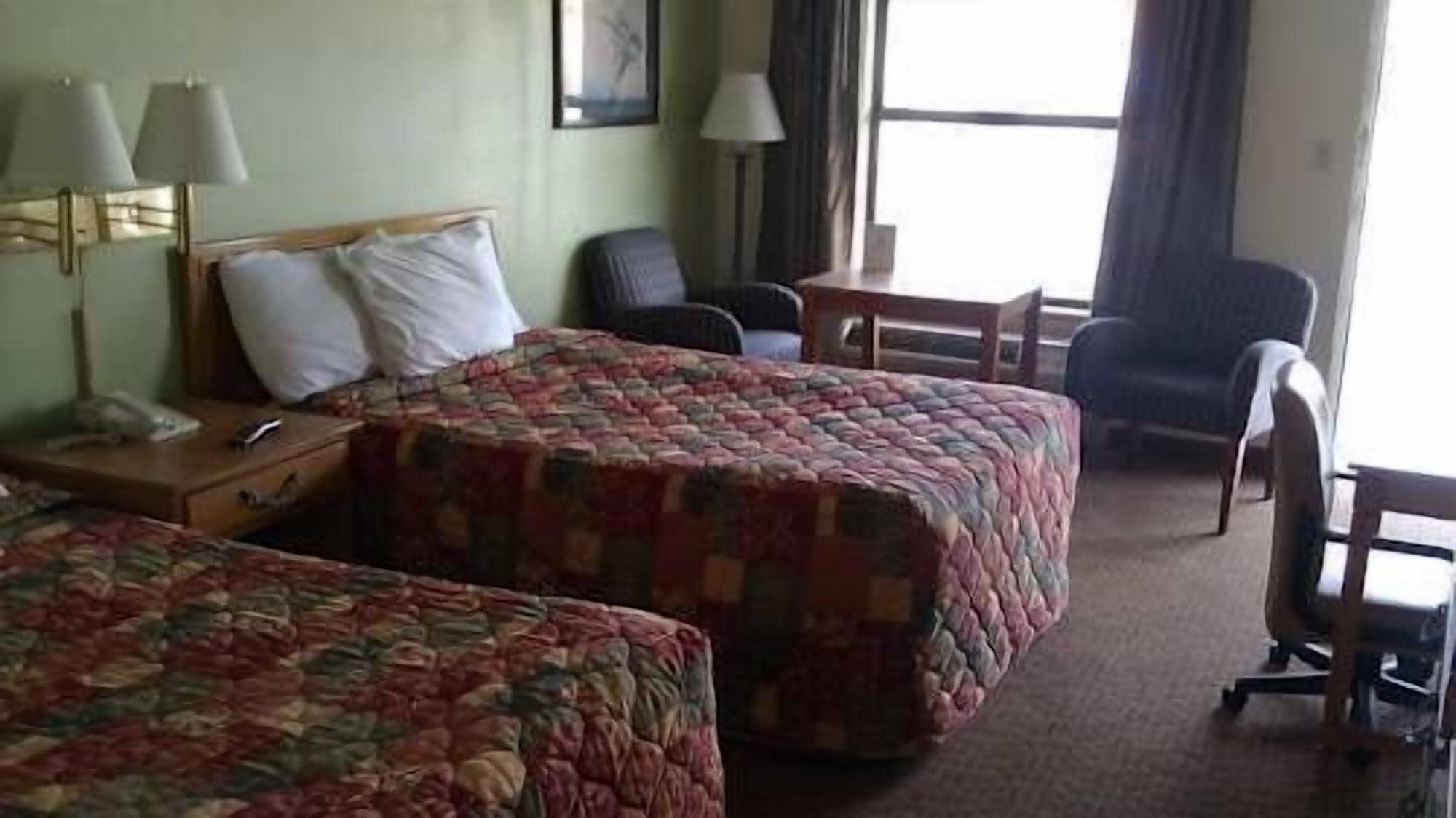 Quarto de hotel com duas camas, uma escrivaninha, uma cadeira e um abajur.