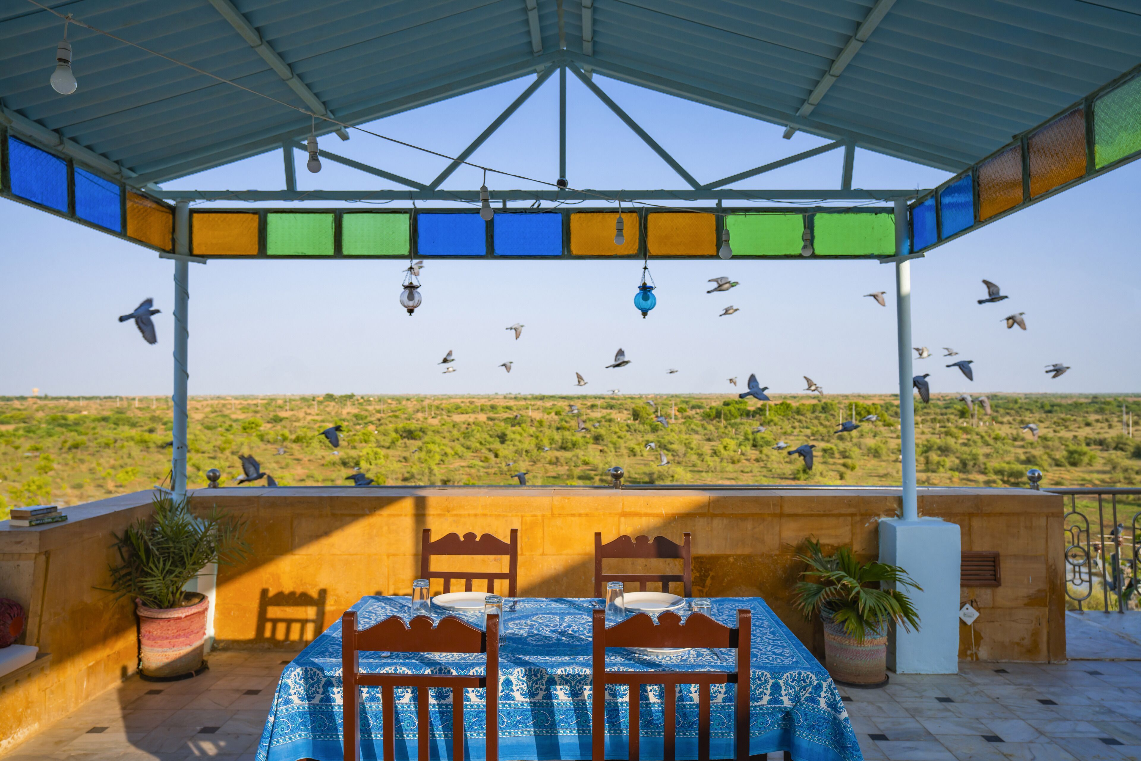 Terraço com mesa e cadeiras, plantas em vasos e vista para uma paisagem verde.