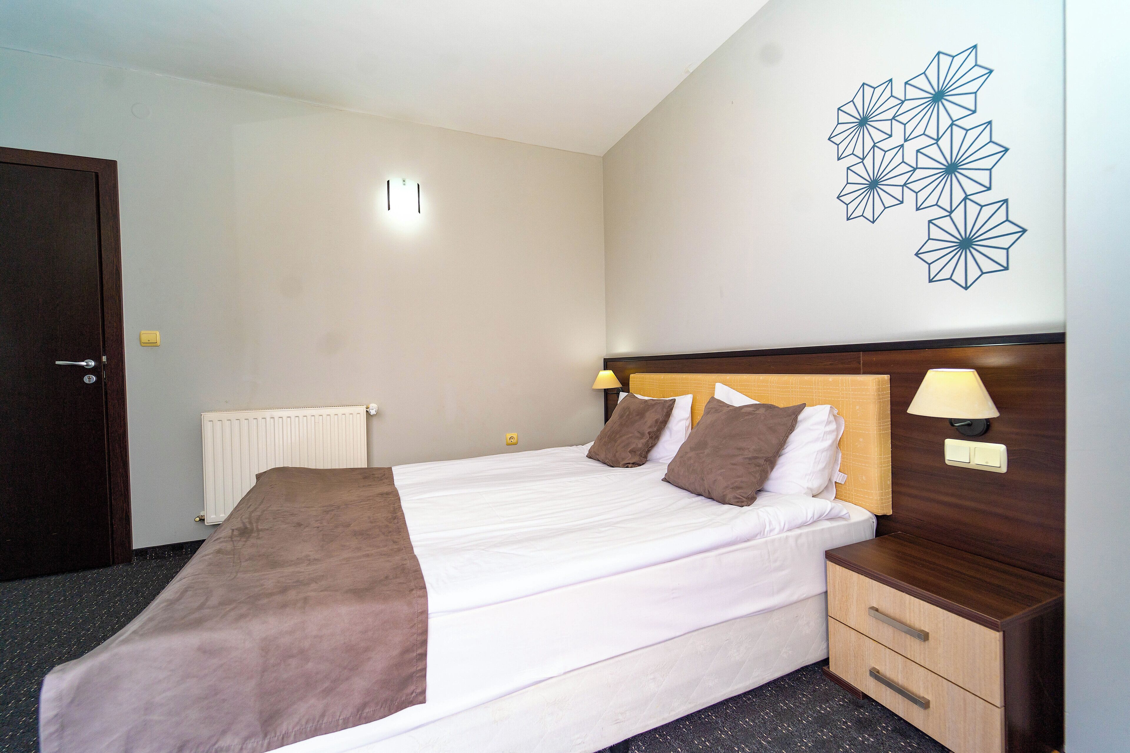 Cama bem arrumada com cabeceira, mesas de cabeceira e um detalhe decorativo na parede.
