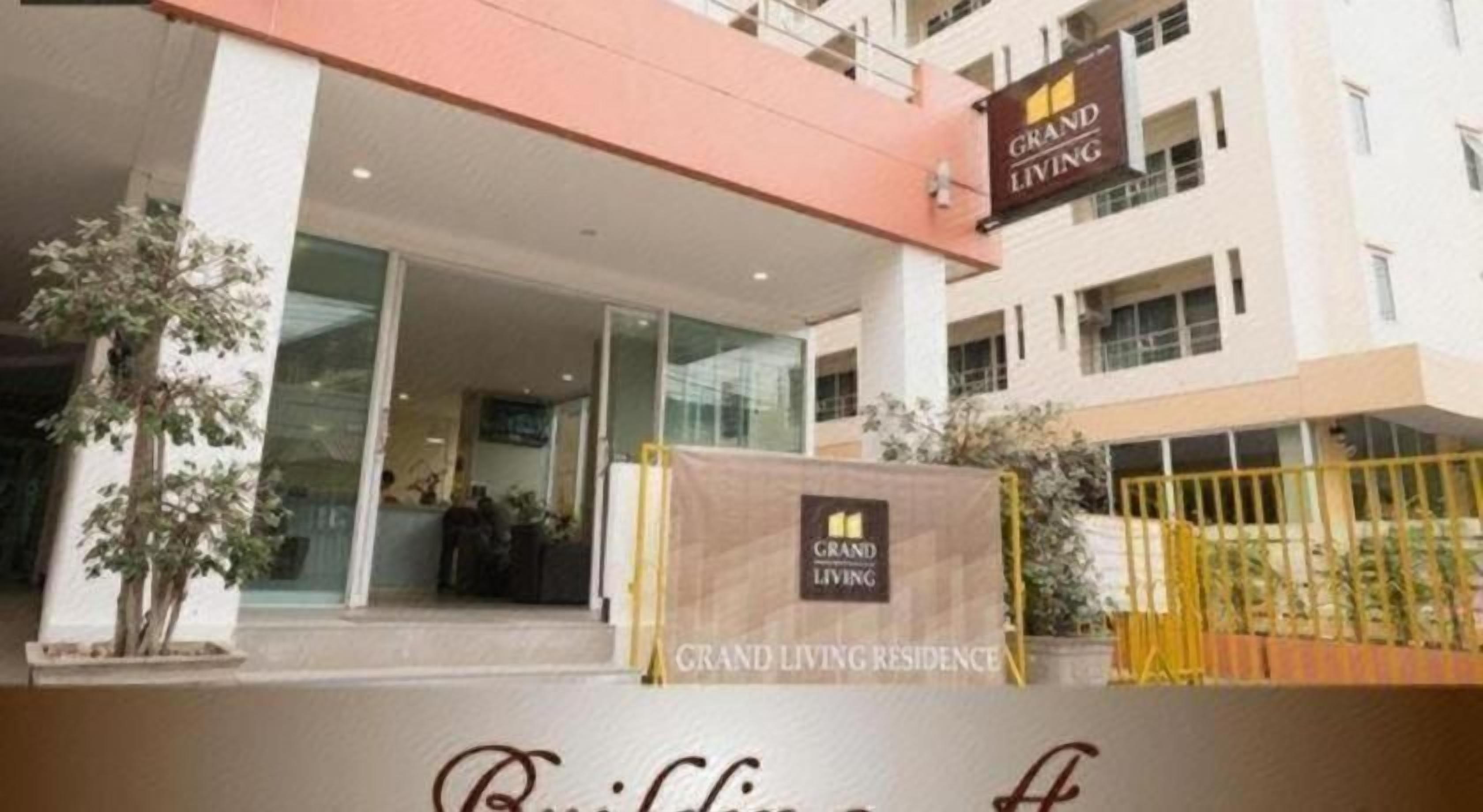 Fachada de vidro do edifício Grand Living Residence, com área de recepção e entrada com portão.