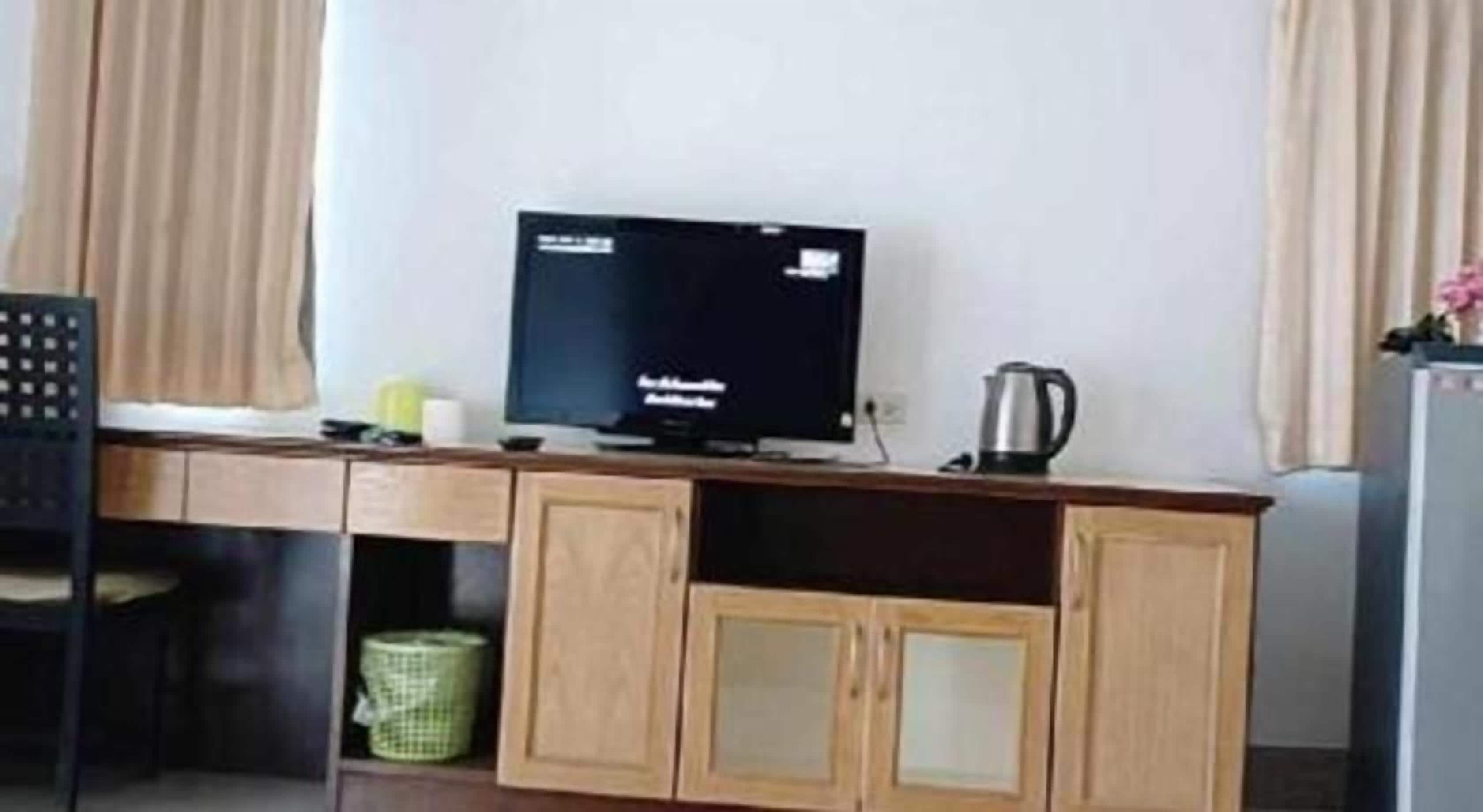Quarto com escrivaninha de madeira, televisão, chaleira e pequeno armário.